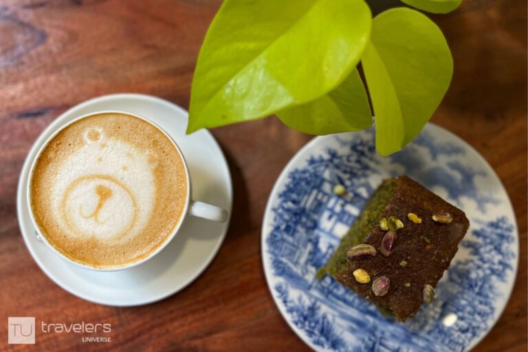 A bear latte art coffee and a slice of pistachio cake on a wooden table at Cult Café