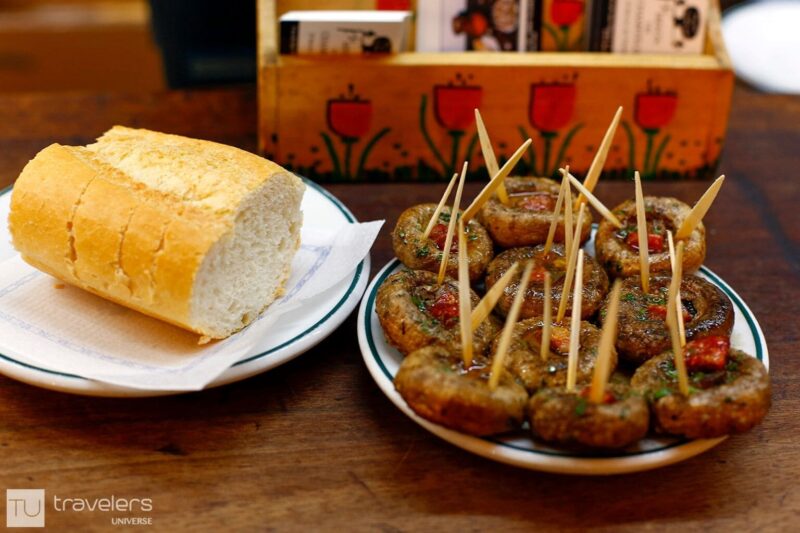 Stuffed mushrooms on a plate with toothpicks pierced through and bread on a wooden table