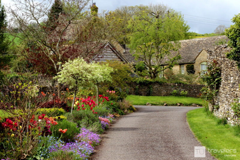 Spring flowers and dry wall lining a little road leading to honey-colored houses in Lower Slaughter