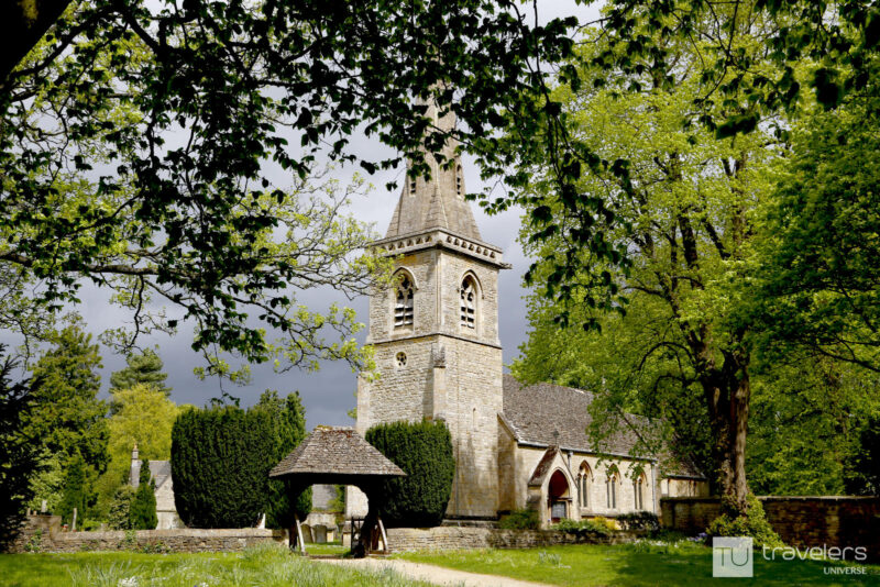 Stone parish church with a tall spire and greenery all around in Lower Slaughter