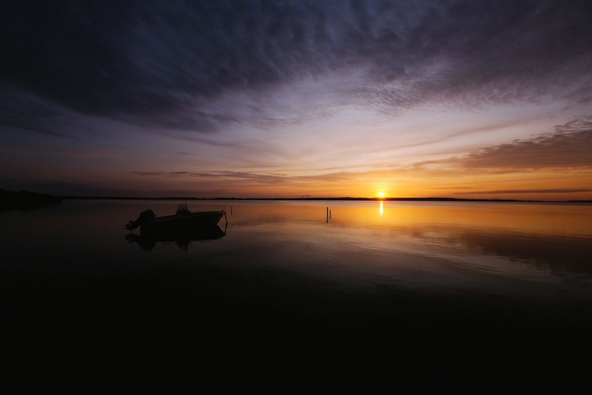 A boat silhouetted against golden sunset reflections on a calm lake similar to Albufera Natural Park