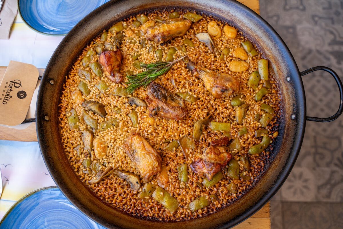 Traditional Valencian paella with chicken, vegetables, and rosemary cooked in a wide pan