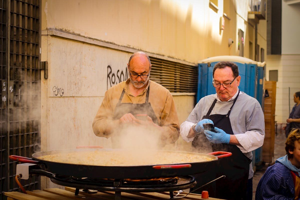 Two chefs cooking a large paella outdoors