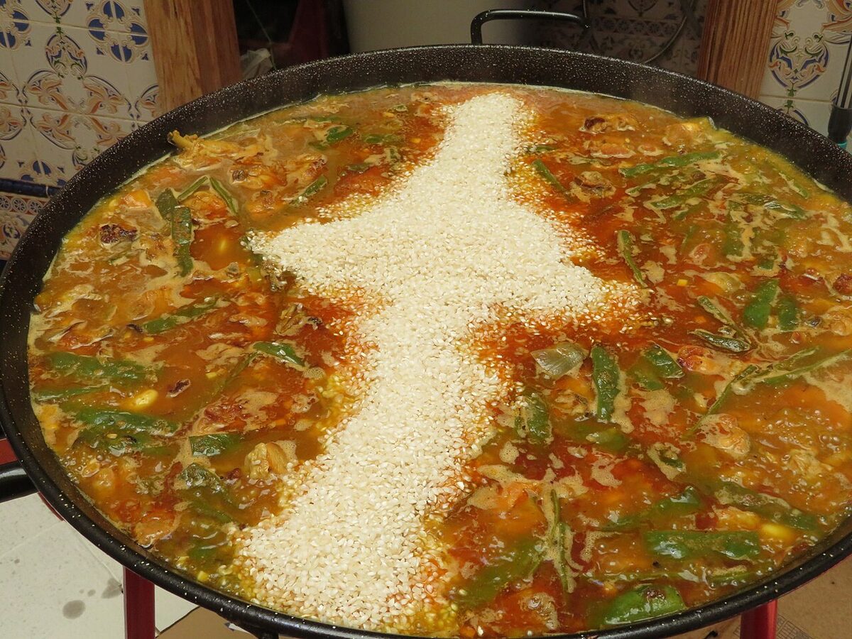 Adding rice to a paella Valenciana cooking over open fire