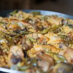 Traditional Valencian paella with rabbit, chicken, and artichokes in a wide pan