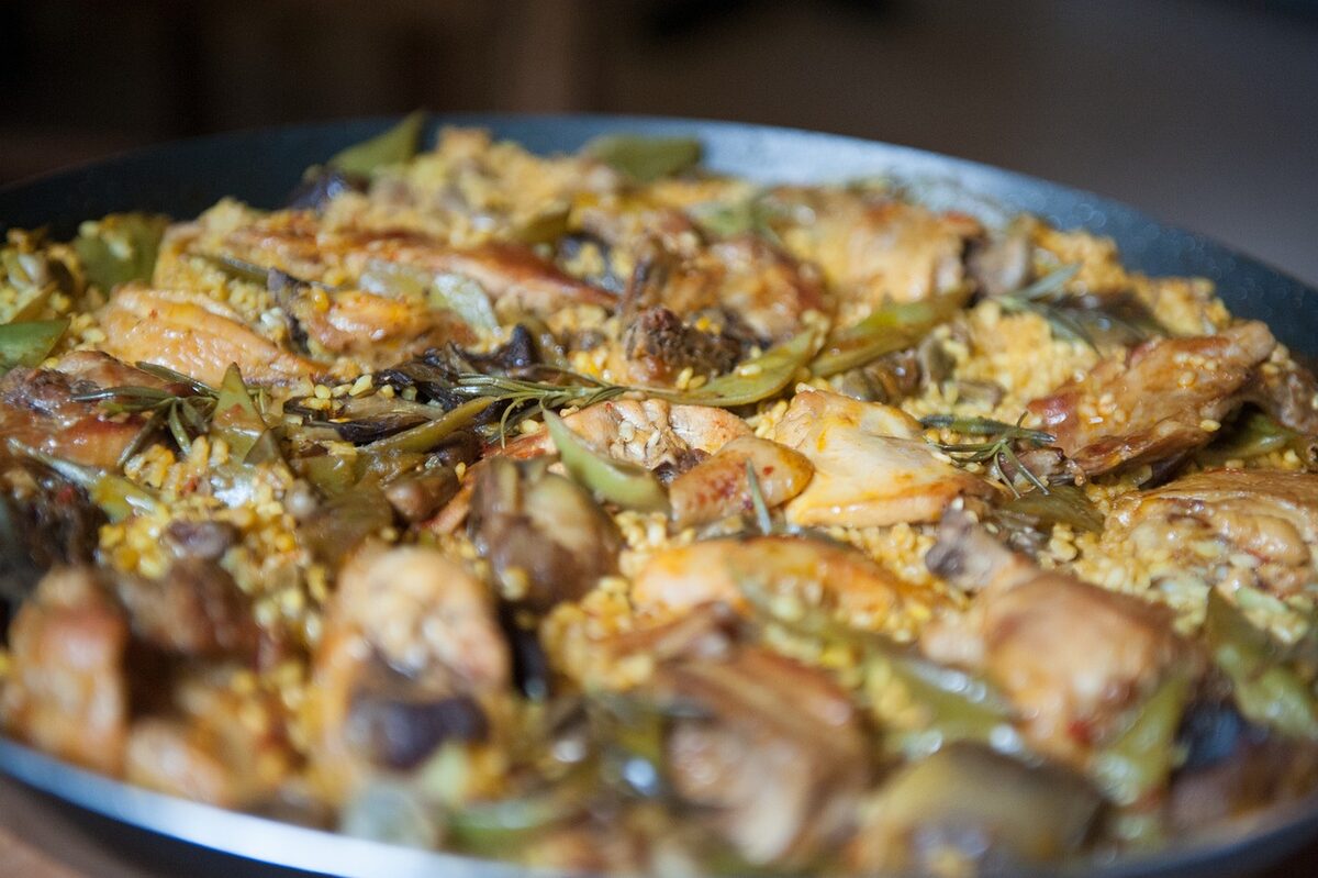Traditional Valencian paella with rabbit, chicken, and artichokes in a wide pan