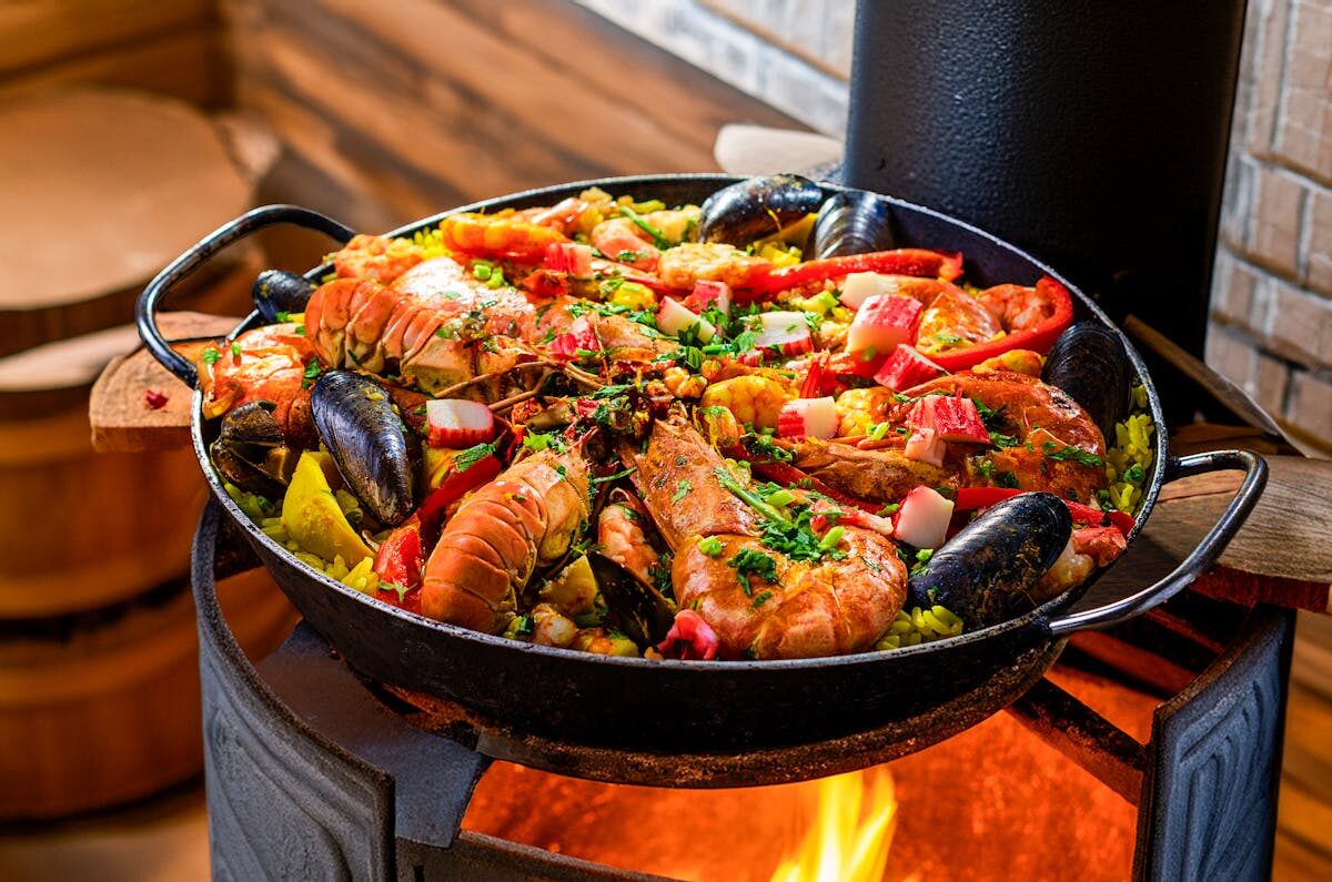 Seafood paella cooking over an open flame with colorful ingredients