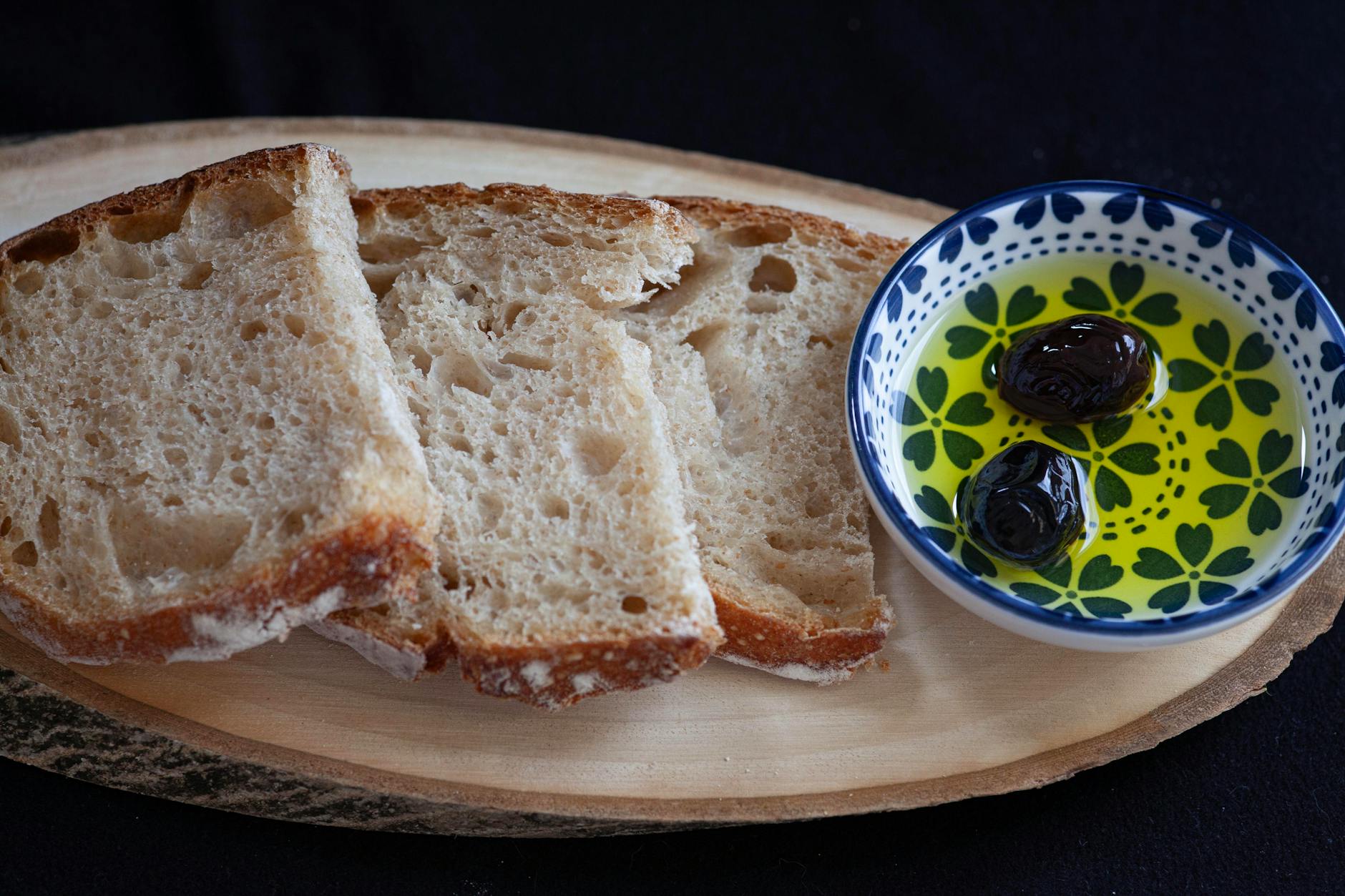 Sliced bread with a dish of olive oil and green olives on a wooden board