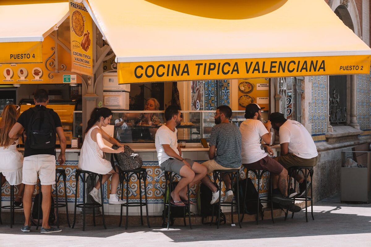 People enjoying food at a Valencian street stall under a bright yellow awning