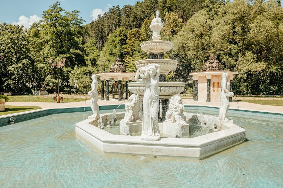 Marble fountain surrounded by classical statues in a landscaped park setting