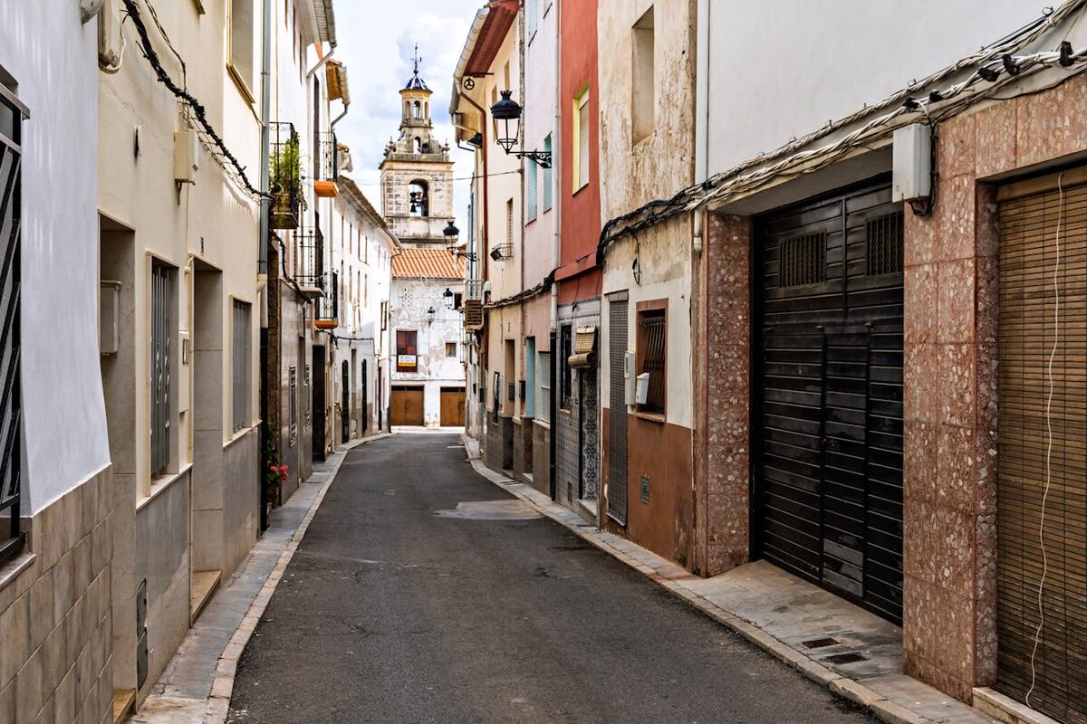 Stone paved narrow alley leading past old buildings with a church tower visible in the background