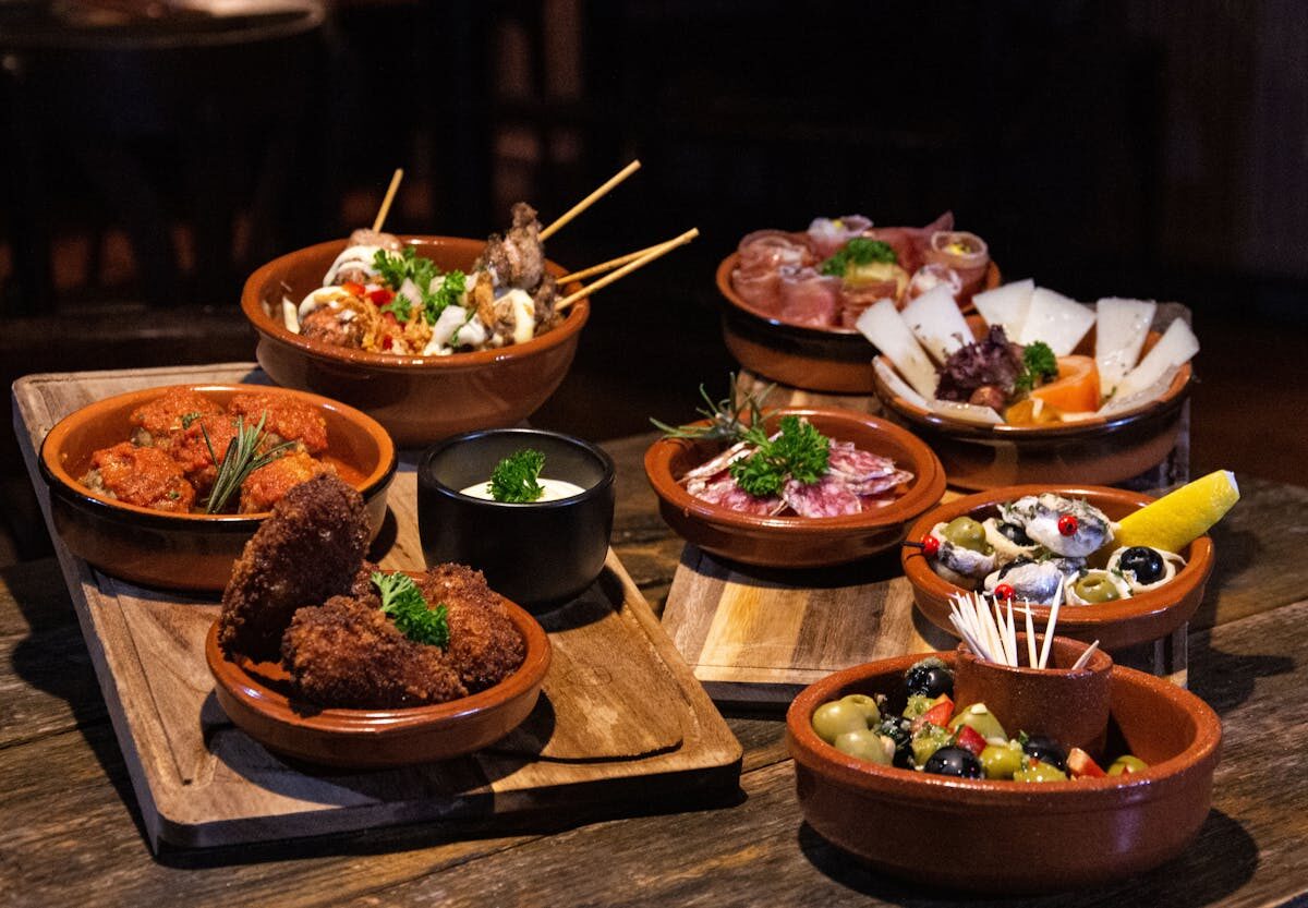 Multiple plates of Spanish tapas dishes arranged on a rustic wooden table