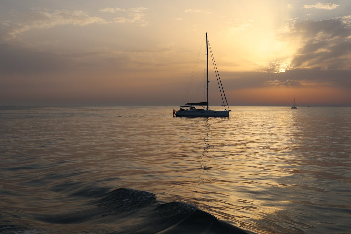 A peaceful sailboat gliding through calm waters at sunset on the Spanish Mediterranean coast