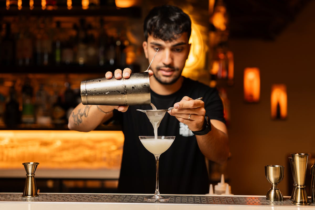 Bartender pouring a cocktail through a strainer at a bar counter