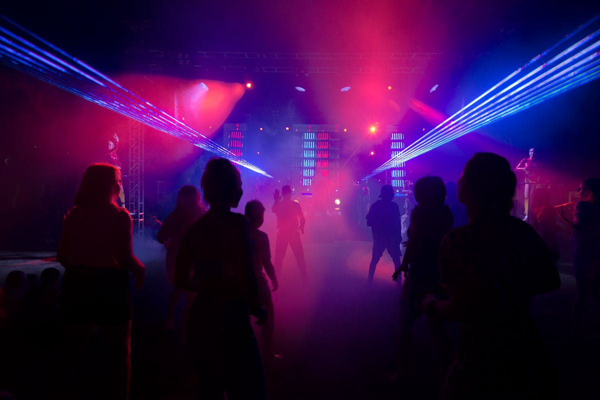 Dance floor illuminated by colorful laser lights with silhouettes of people dancing