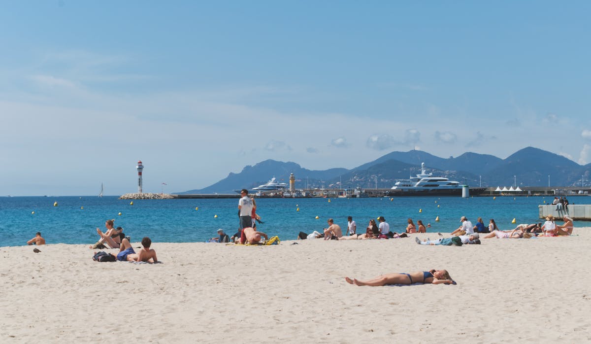 Sunny day at Cannes beach with yachts anchored offshore and a lighthouse in the distance