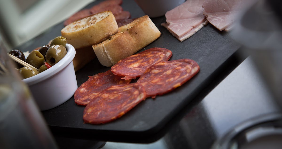 Charcuterie platter with sliced meats, olives, and bread on a slate board
