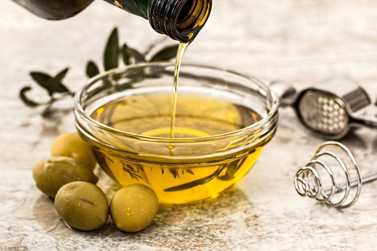 Close-up of olive oil pouring into a glass bowl surrounded by olives