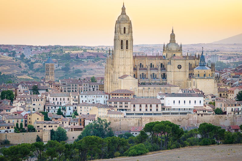 Segovia Cathedral with its Gothic spires silhouetted against a colorful sunset sky