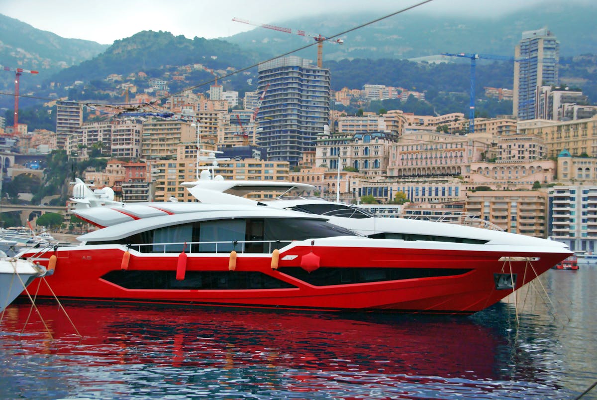 A red yacht docked in the Monaco harbor with city buildings in the background