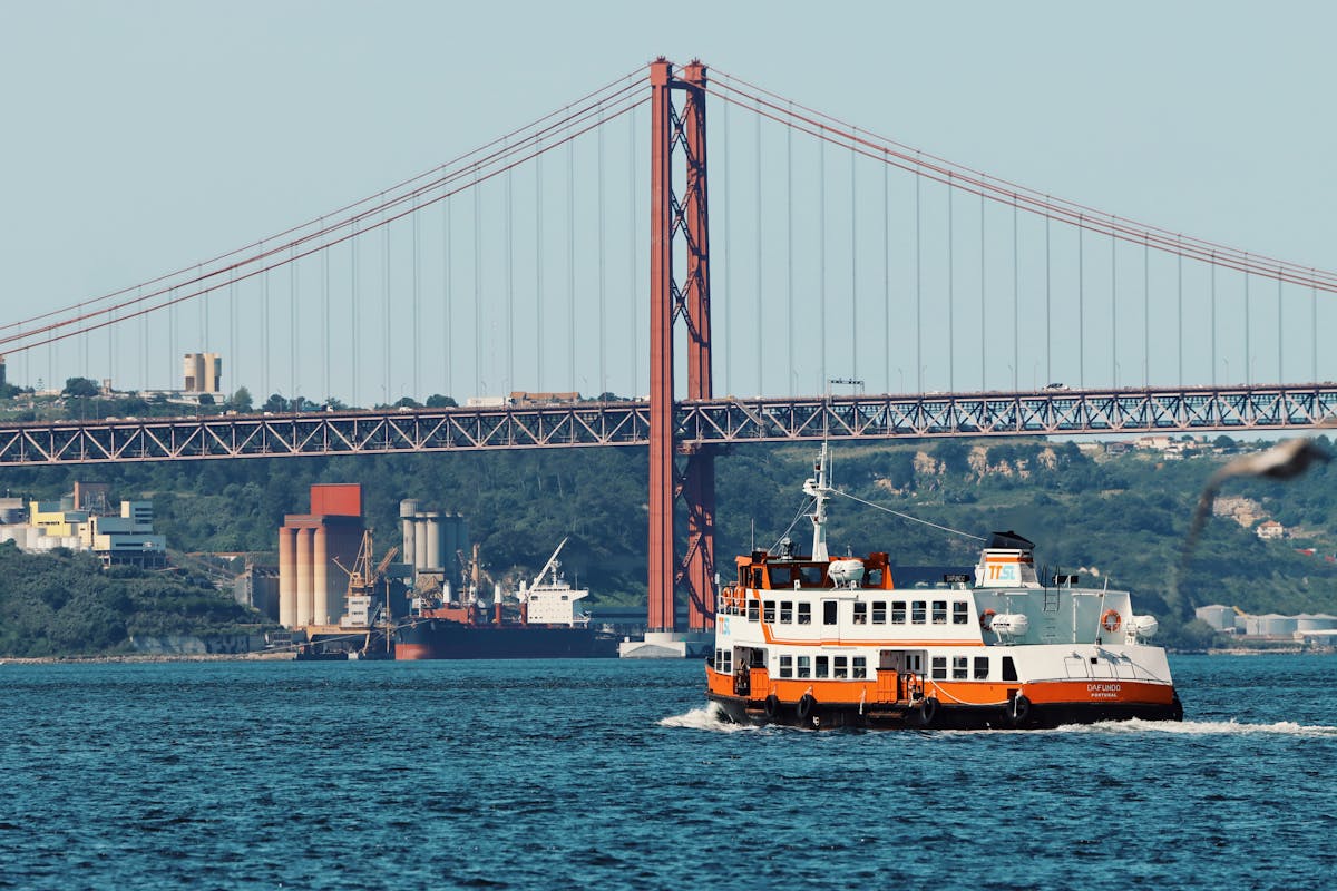 The 25 de Abril Bridge in Lisbon with a passenger ferry on the Tagus River