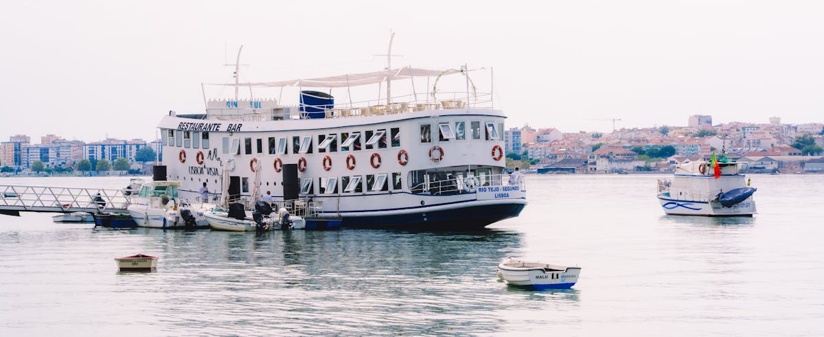 A floating restaurant vessel on the Tagus River in Lisbon with the city skyline behind