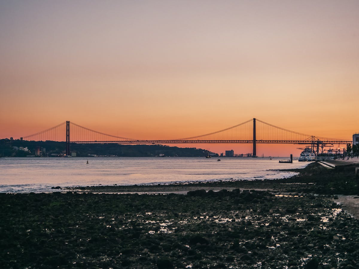 The 25 de Abril Bridge silhouetted against an orange sunset reflected on the Tagus River