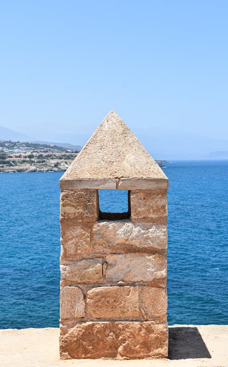A historic stone tower overlooking the Mediterranean Sea in Rethimno, Greece, under a clear blue sky.