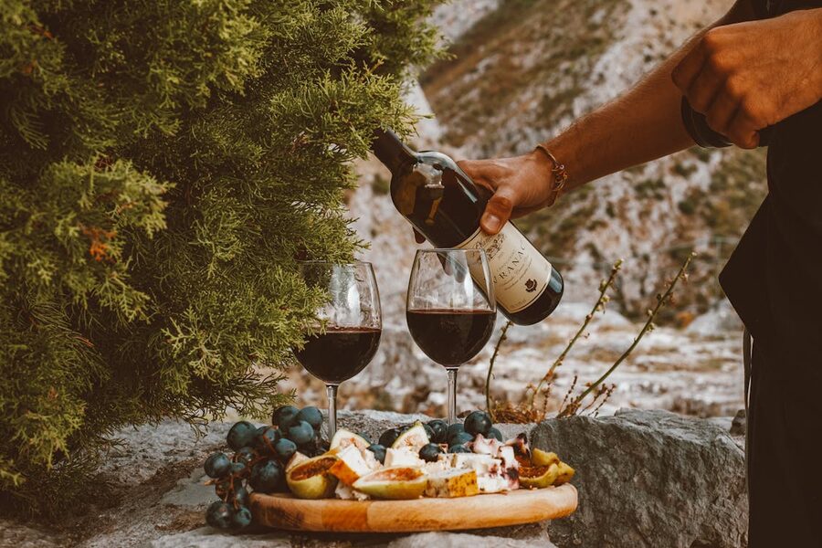 A scenic outdoor setting with red wine, cheese, and grapes on a stone surface.
