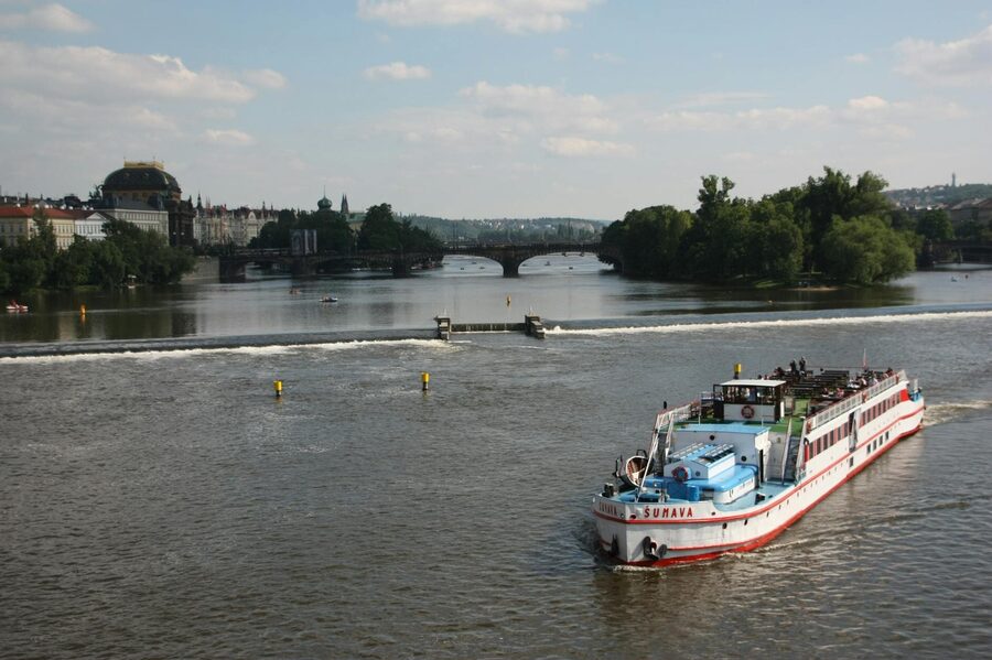 A riverboat cruises on the Vltava River with historic Prague architecture on both banks