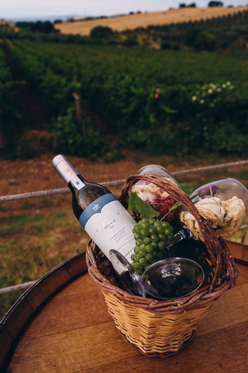 A scenic vineyard picnic with wine, grapes, and fresh bread in a basket.