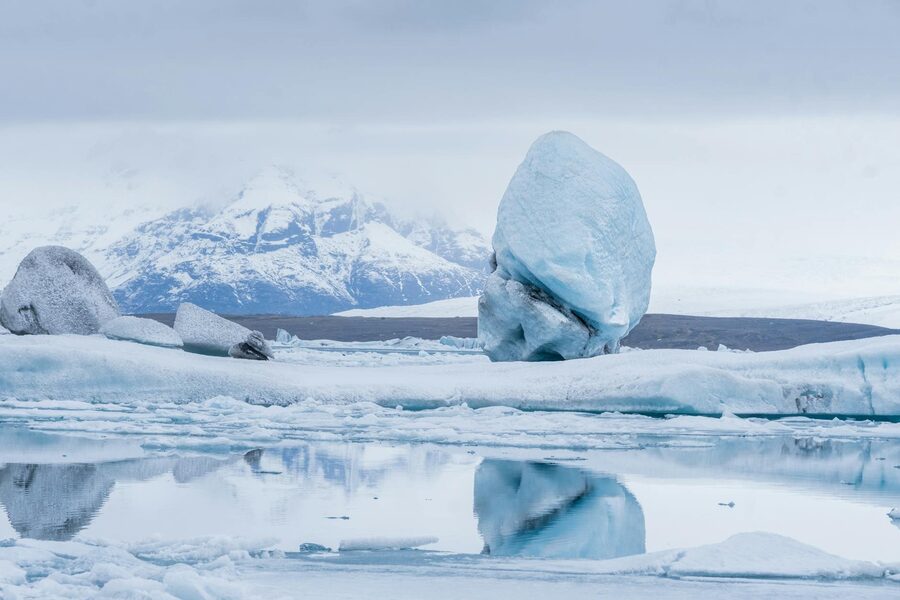 A stunning view of a glacier and snowy mountain reflected in a pristine icy lagoon under a winter sk