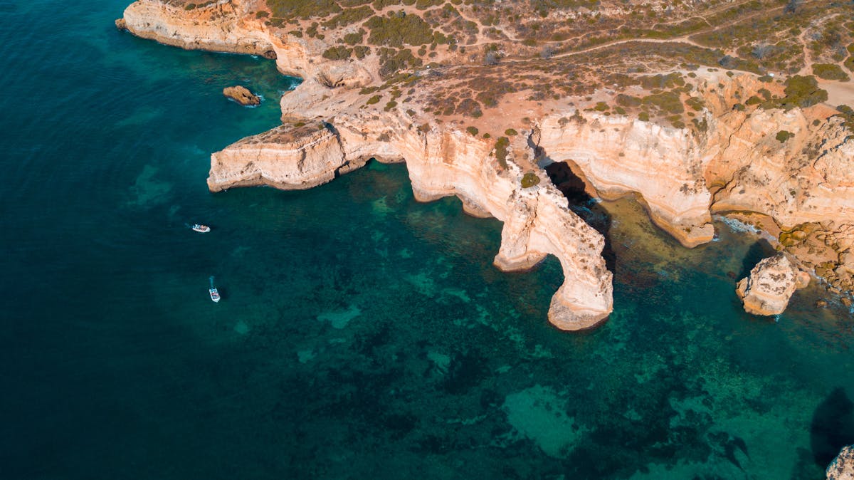 Aerial view of cliffs and boats along the blue ocean shore in Algarve