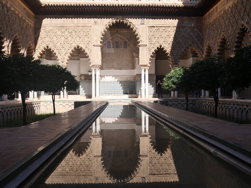 Intricate Moorish architecture reflected in water at the Alcazar of Seville