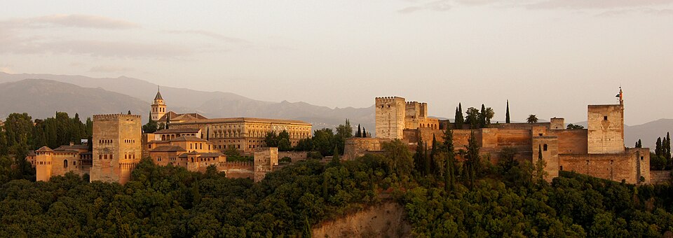 The Alhambra palace complex lit up at dusk against a darkening sky
