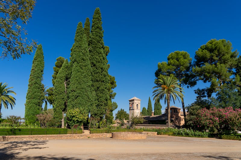 Gardens and fortress walls of the Alhambra under a clear blue sky in Granada