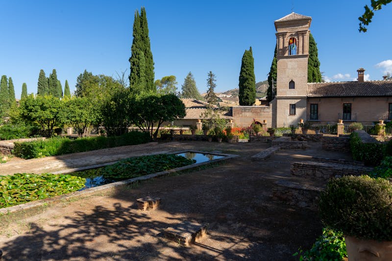 Lush green gardens with historic Alhambra buildings and tower in background