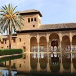 The Alhambra Palace reflected in a still pool with palm trees in Granada Spain