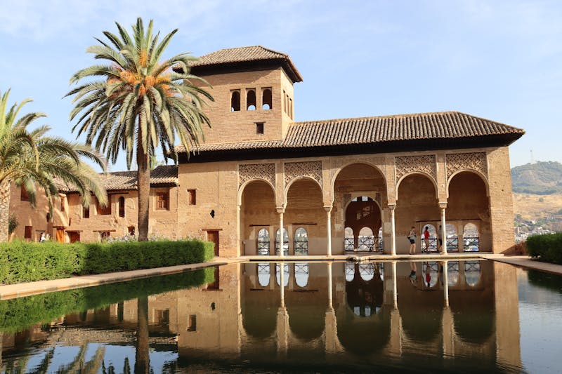 The Alhambra Palace reflected in a still pool with palm trees in Granada Spain