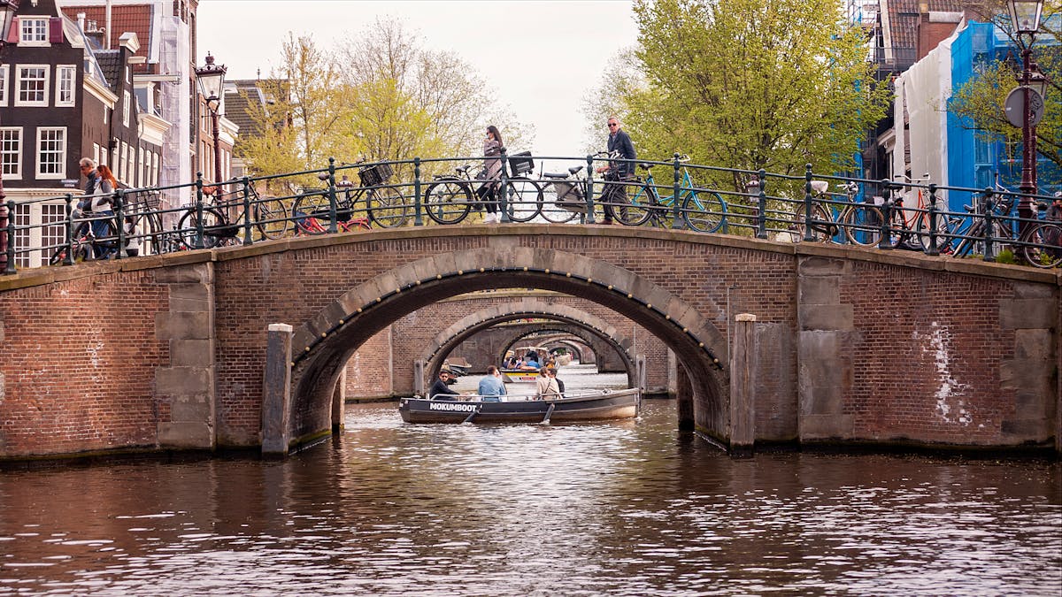 Tourists and bicycles on an Amsterdam canal bridge on a sunny day