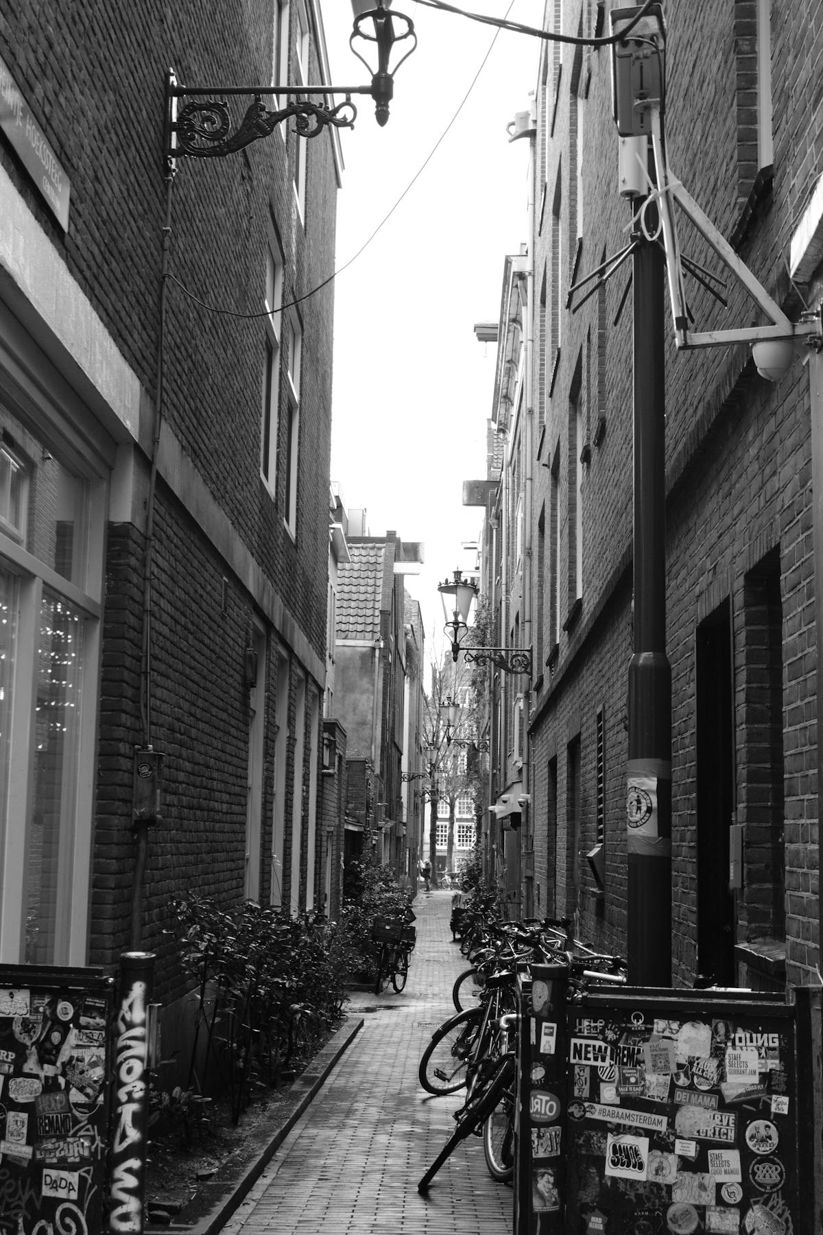 Grayscale view of a narrow Amsterdam alley with bicycles and classic brick buildings