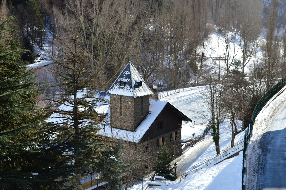 Aerial view of snow-covered church building surrounded by winter forest in La Massana, Andorra