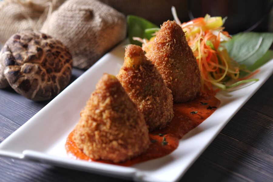 Crispy arancini served on a plate with tomato sauce and fresh salad