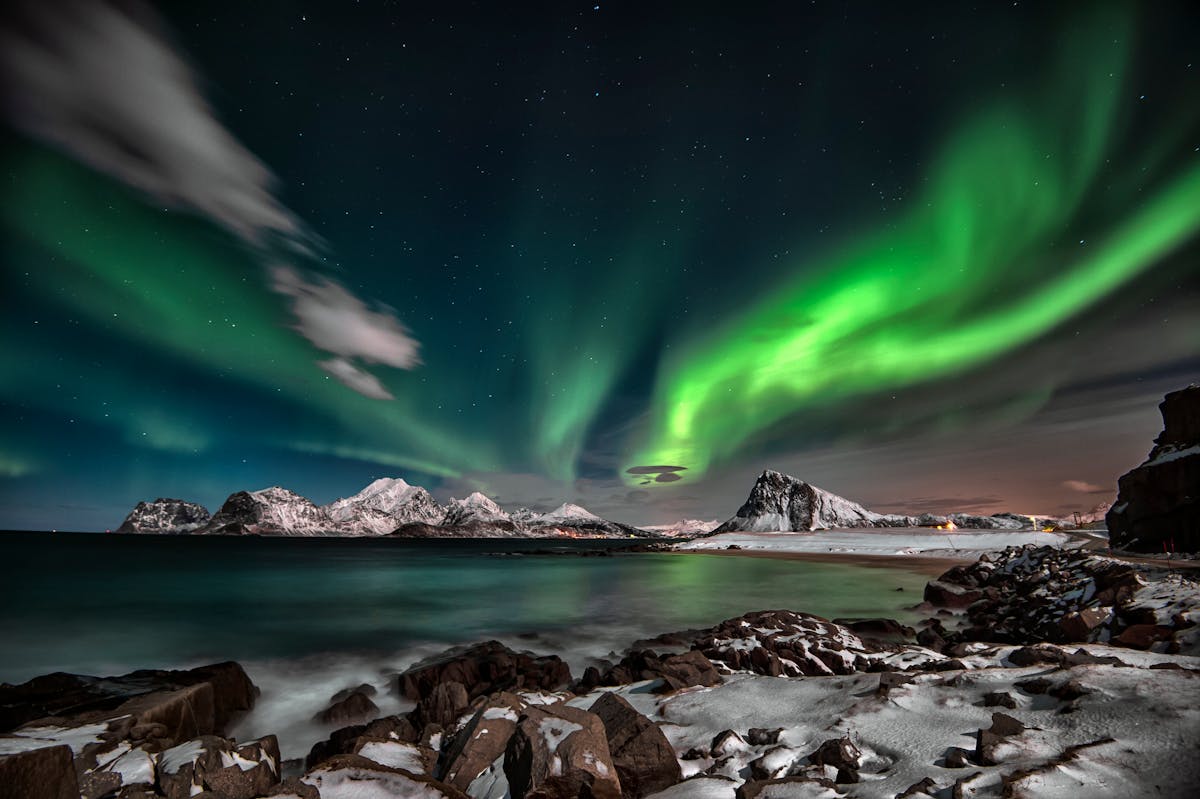 Aurora borealis illuminating a winter landscape with snowy mountains and starry sky