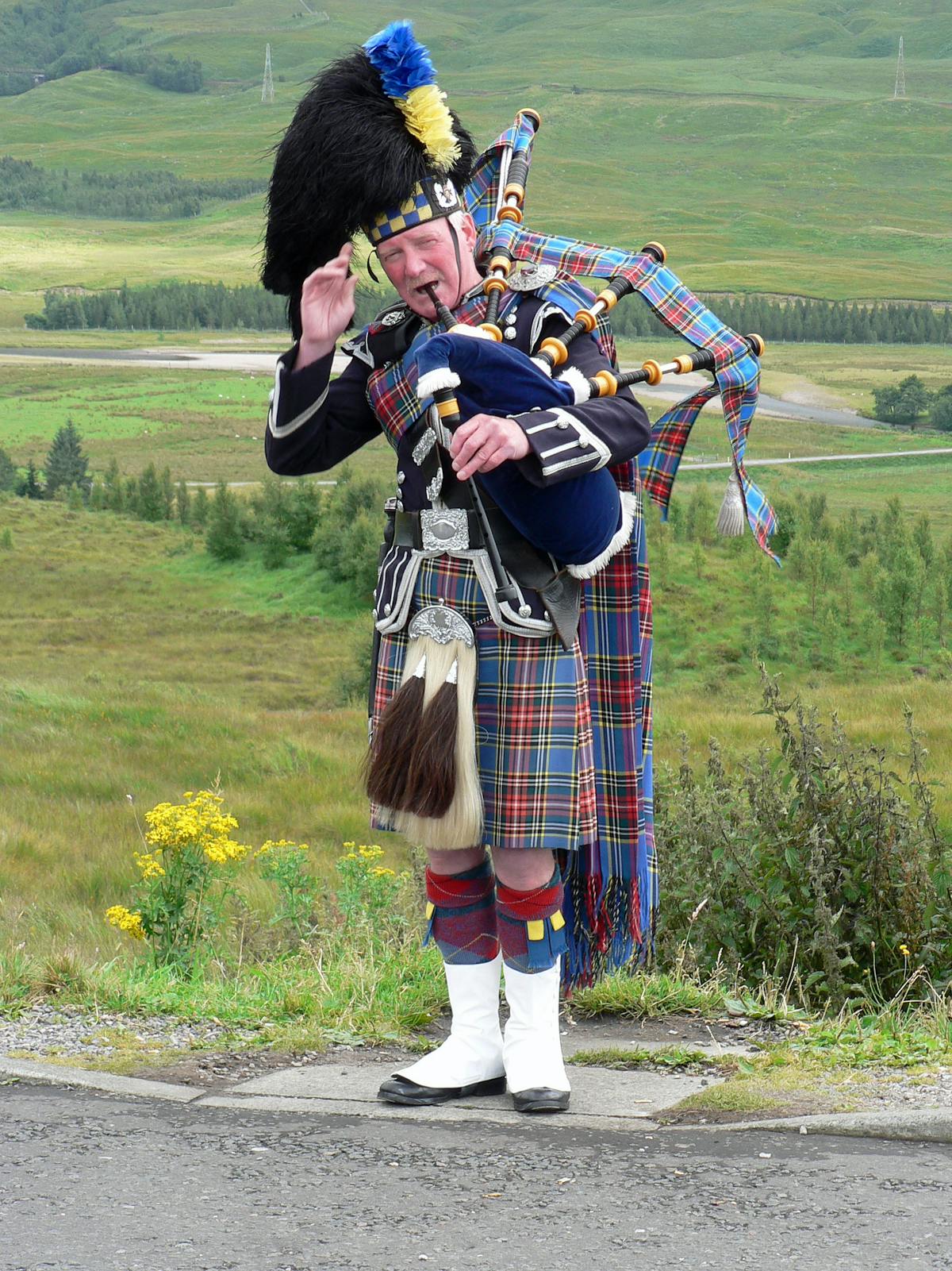 A bagpiper in traditional Scottish attire playing in the Highlands