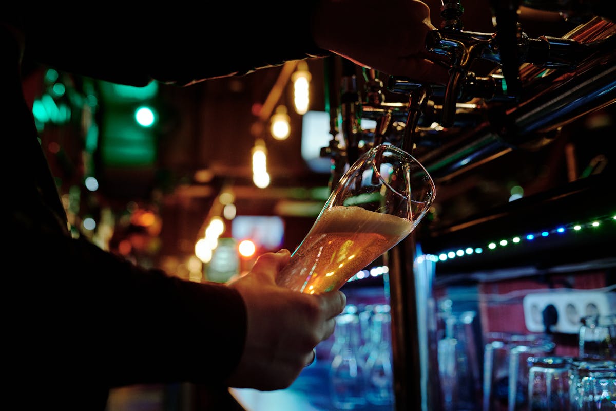 A person pouring beer from a tap into a glass at a dimly lit bar