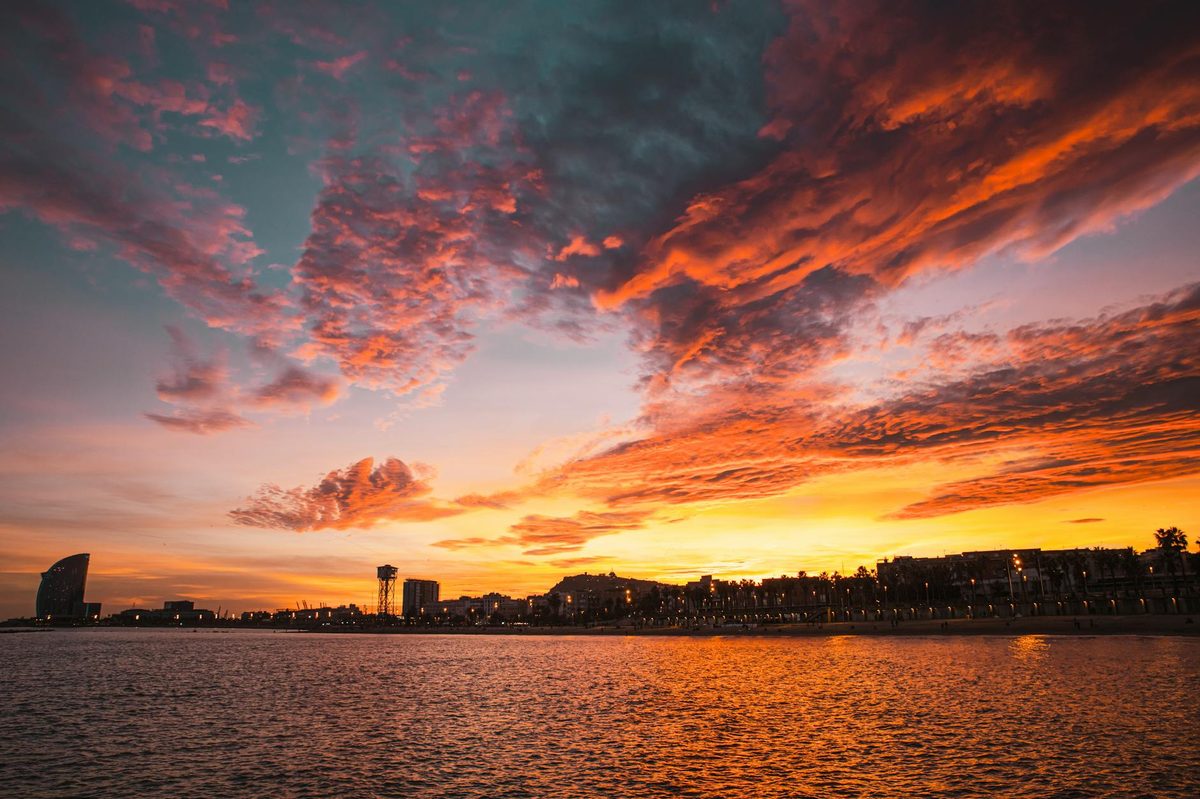 Sunset over Barcelona beach with dramatic clouds and city skyline