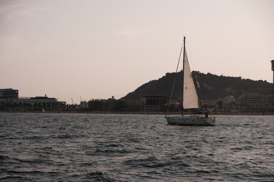 Sailboat cruising along Barcelona coastline with Montjuic hill at sunset