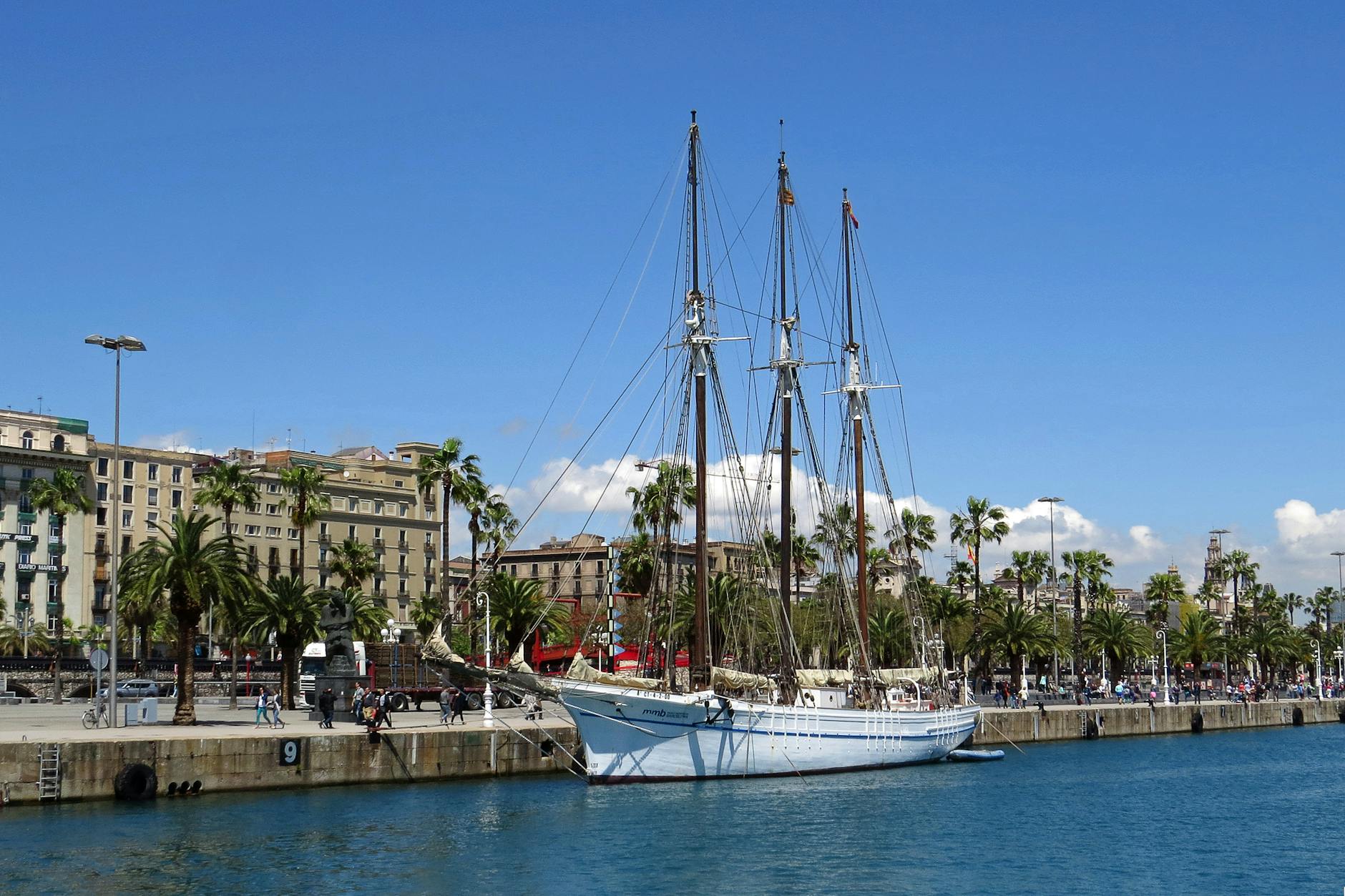 Sailboat docked at Barcelona harbour with a palm-lined street