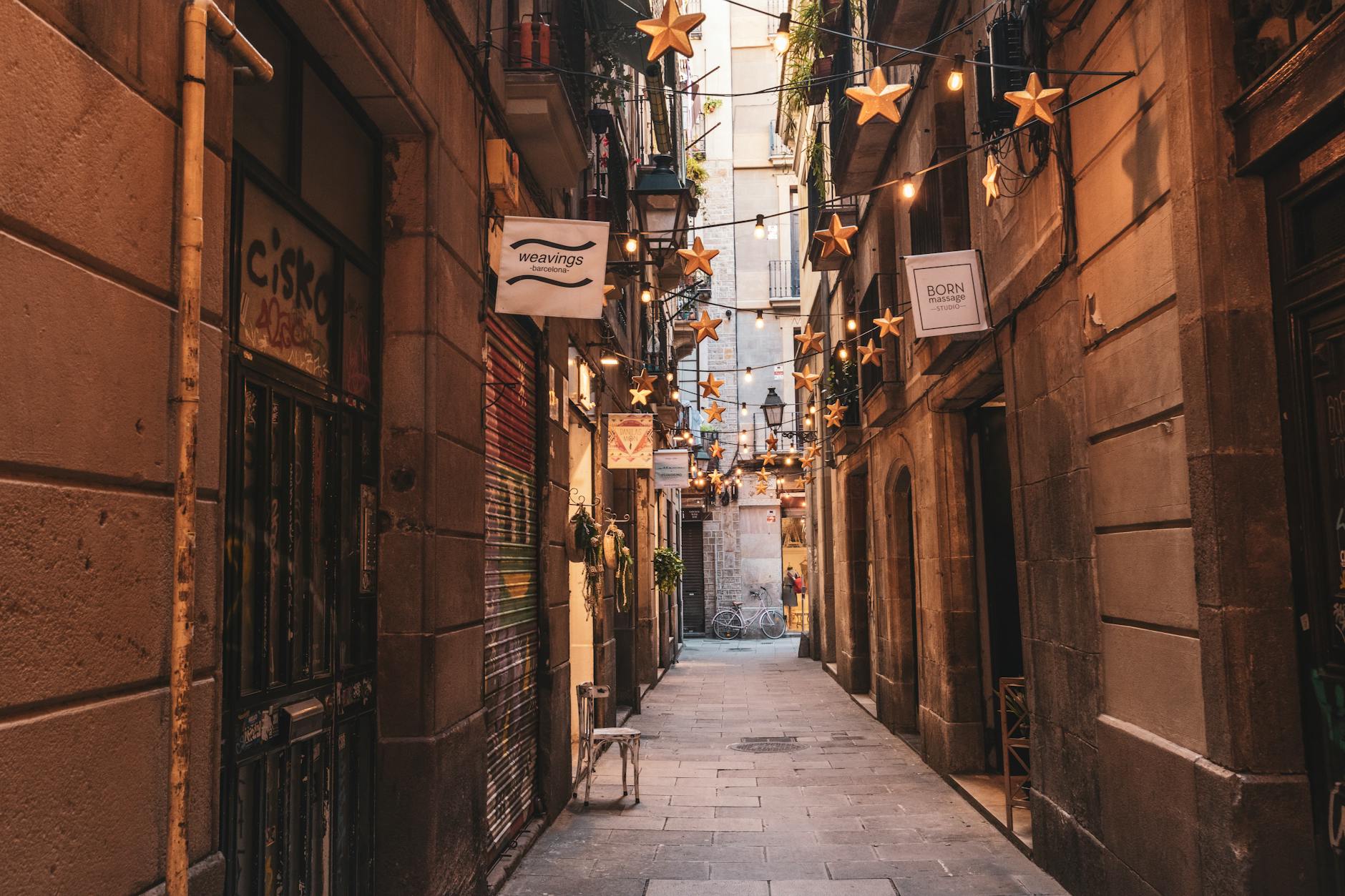 Narrow Barcelona alley adorned with star-shaped string lights between old buildings